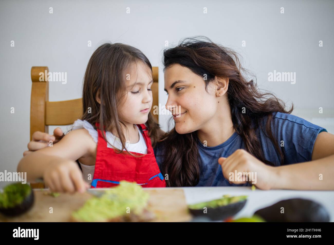 Happy mother hugging daughter while spreading avocado on toast. Cute ...