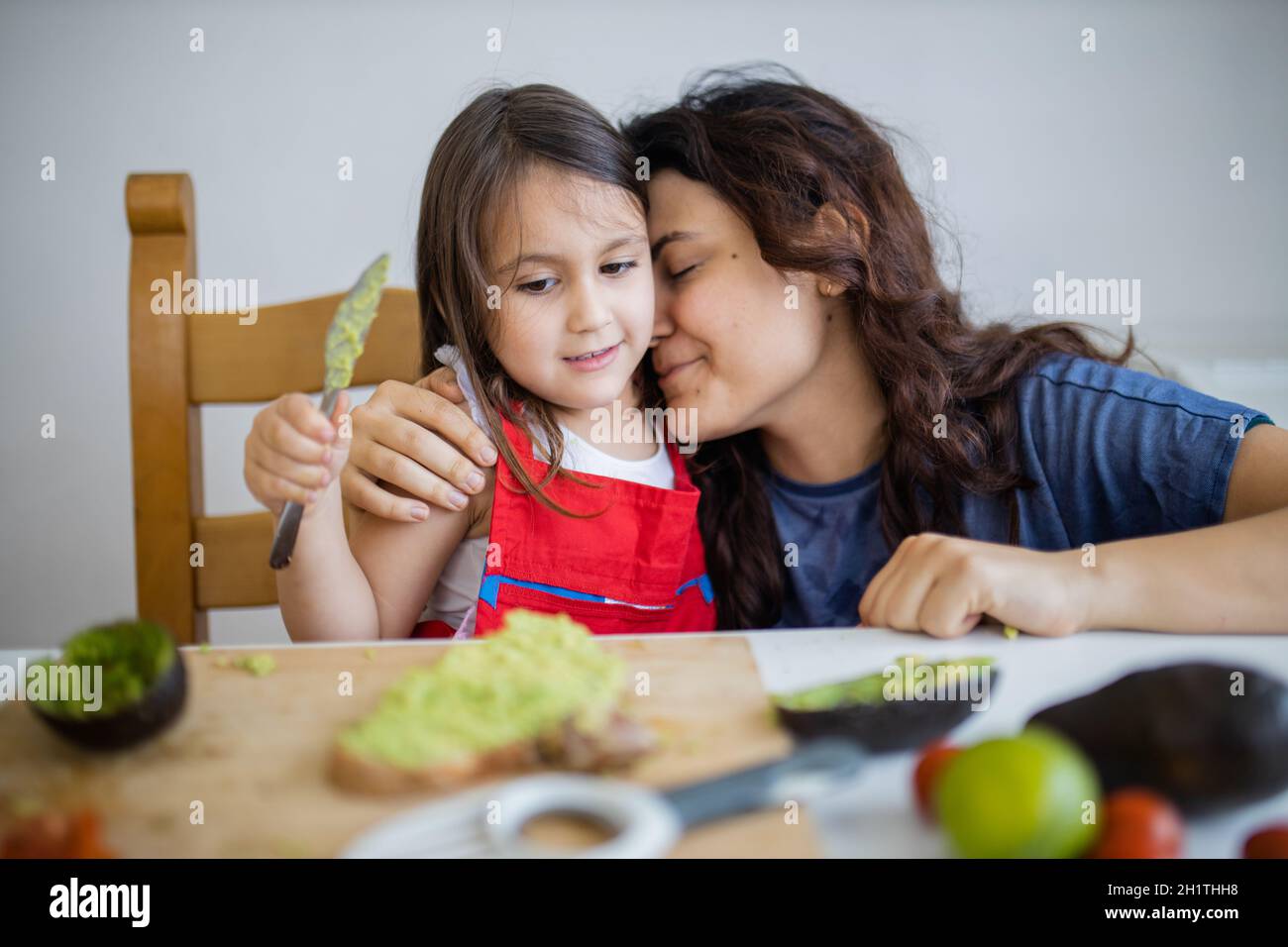 Happy mother hugging daughter while spreading avocado on toast. Cute ...