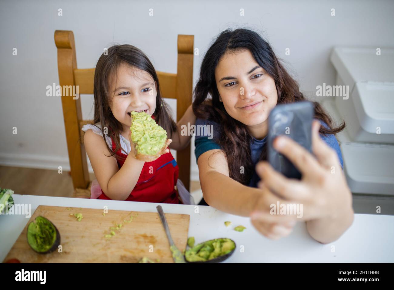 Happy mother and daughter taking selfie while eating toast with avocado ...
