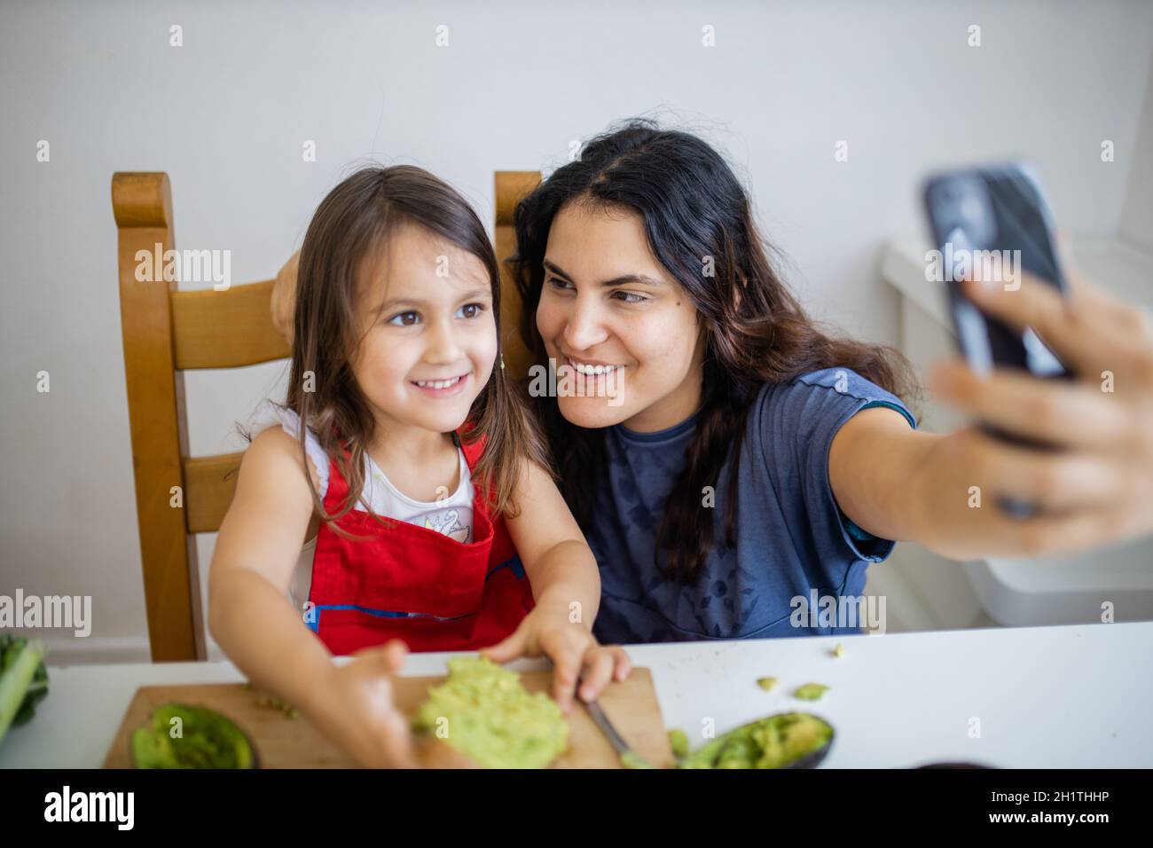 Happy mother and daughter taking selfie while eating toast with avocado ...