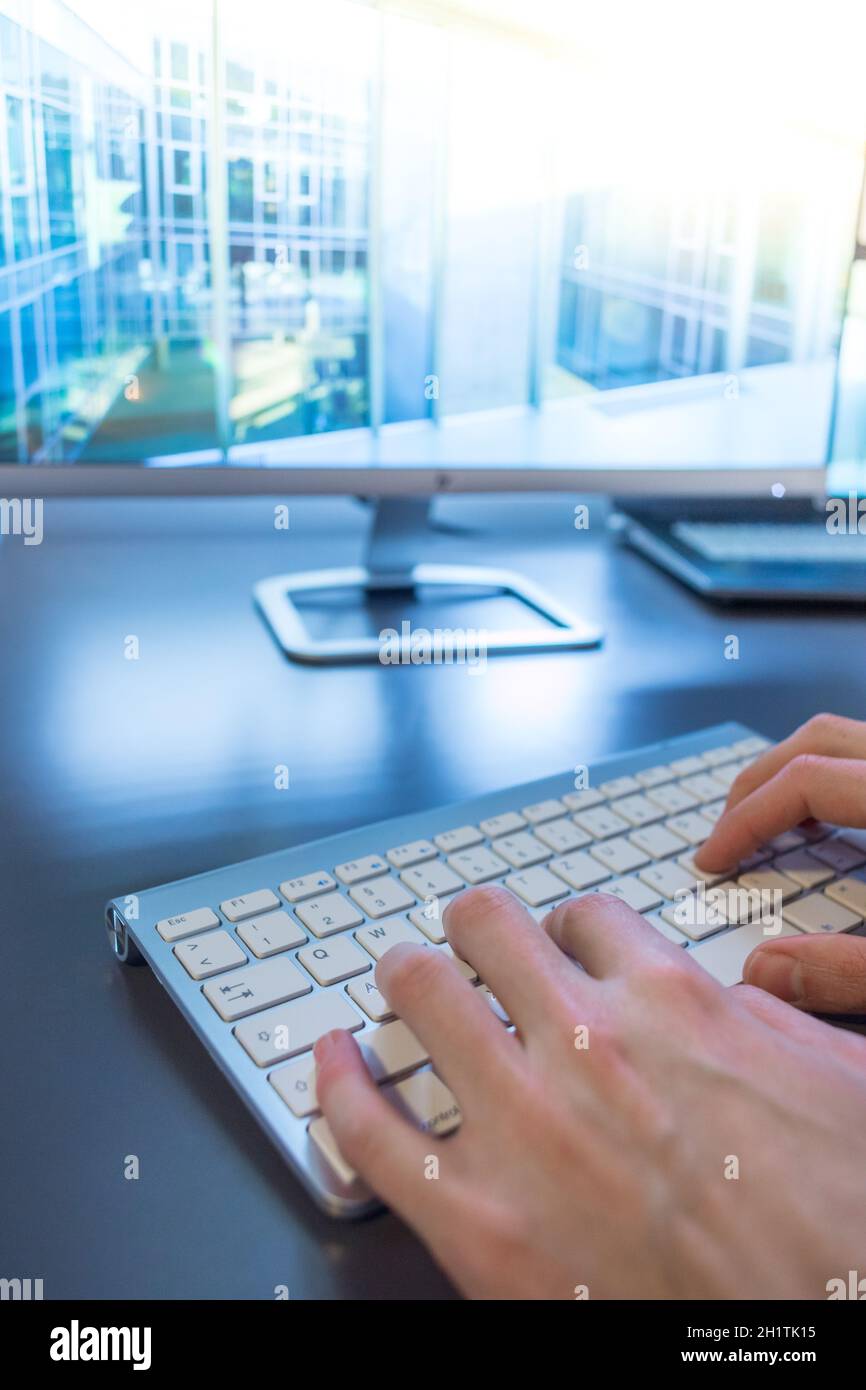 Hands are typing on a white keyboard, screen in the blurry background ...