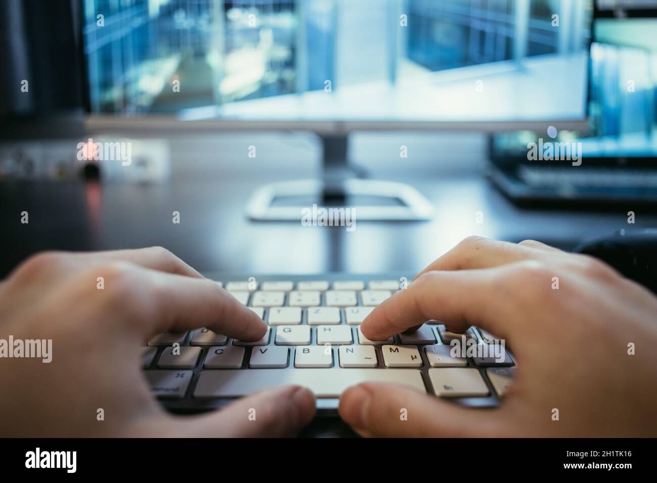 Hands are typing on a white keyboard, screen in the blurry background ...