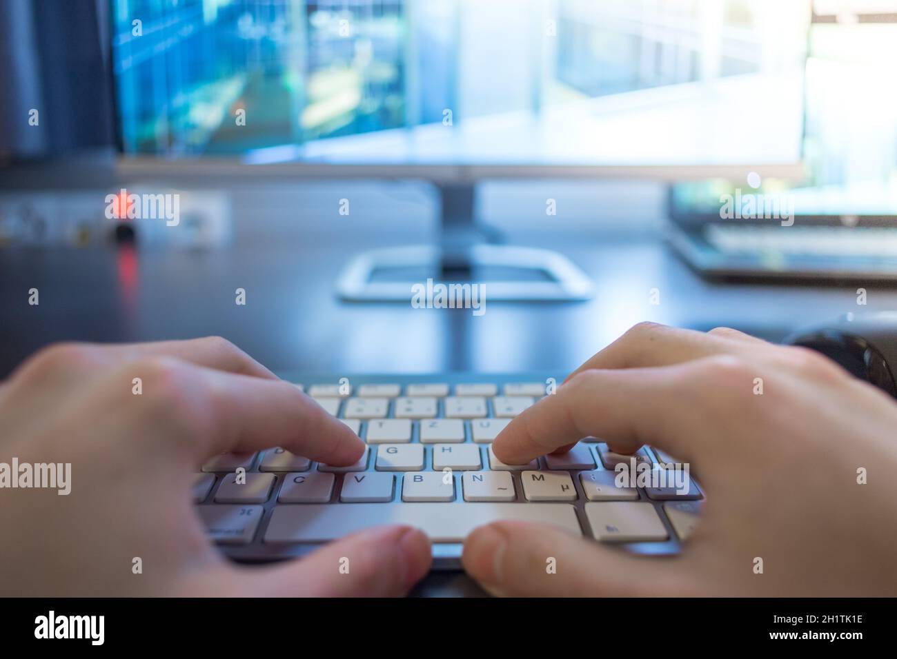 Hands are typing on a white keyboard, screen in the blurry background ...
