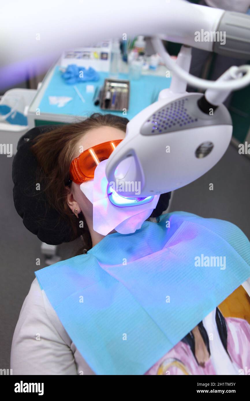 Teeth whitening in dental clinic.Young woman whitens her teeth with ...