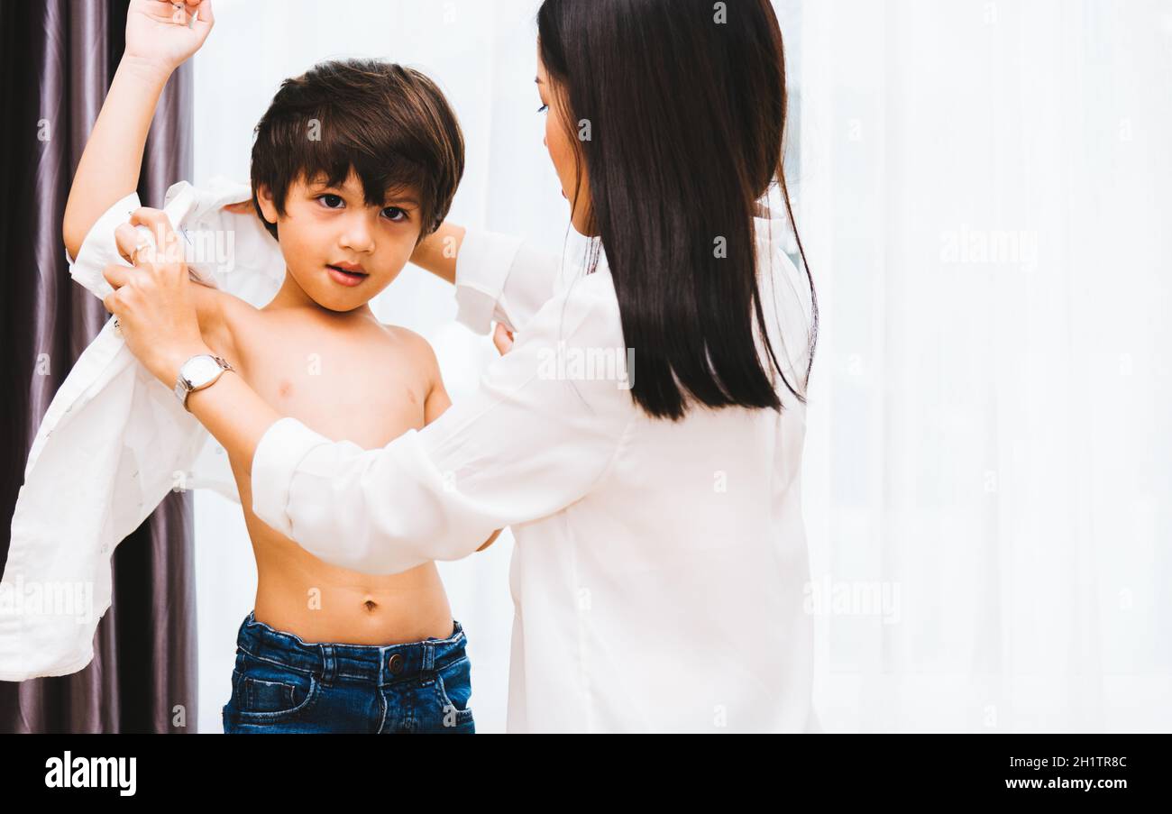 Asian happy beautiful mother helping to get dressed clothes on her boy ...
