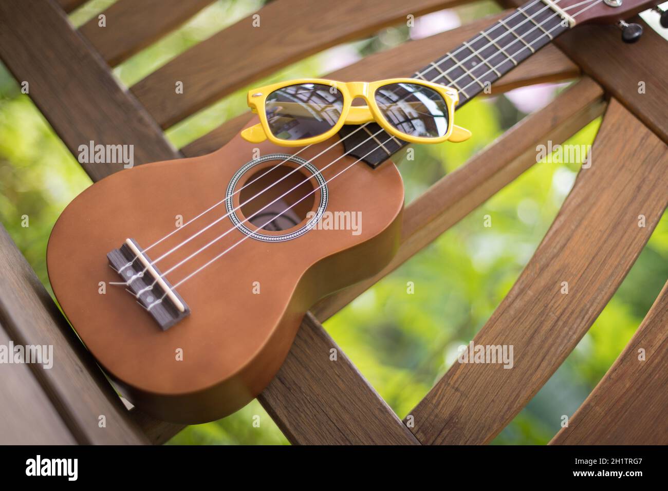 Ukulele and yellow sunglasses on a wooden park bench in summer, green ...