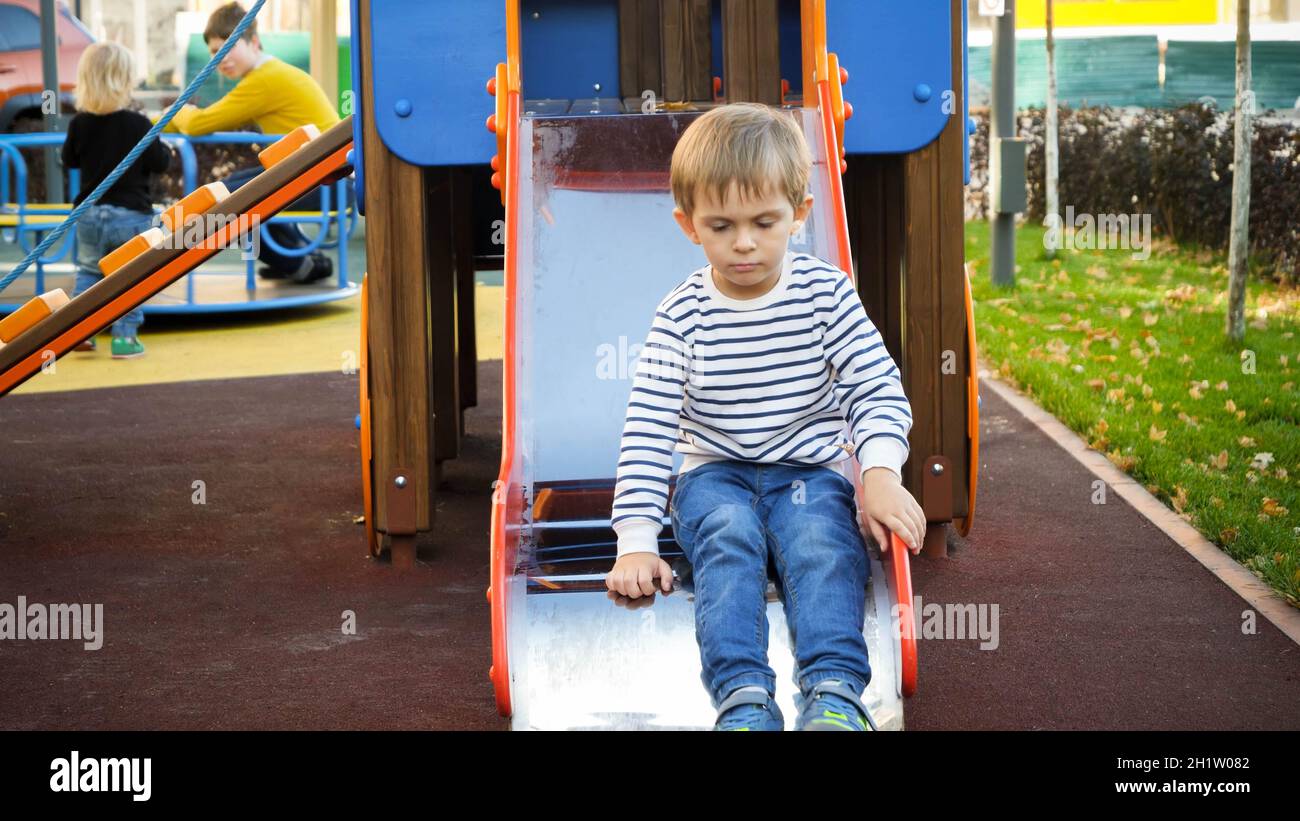 Sad and upset little lonely boy sitting on slide at playground Stock ...