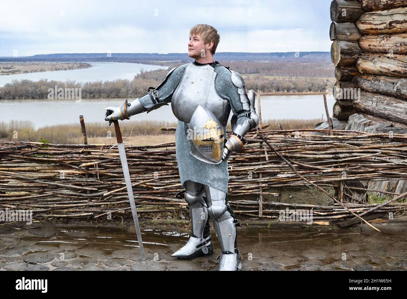 Knight in armor on the background of a wicker fence, a wooden house and ...