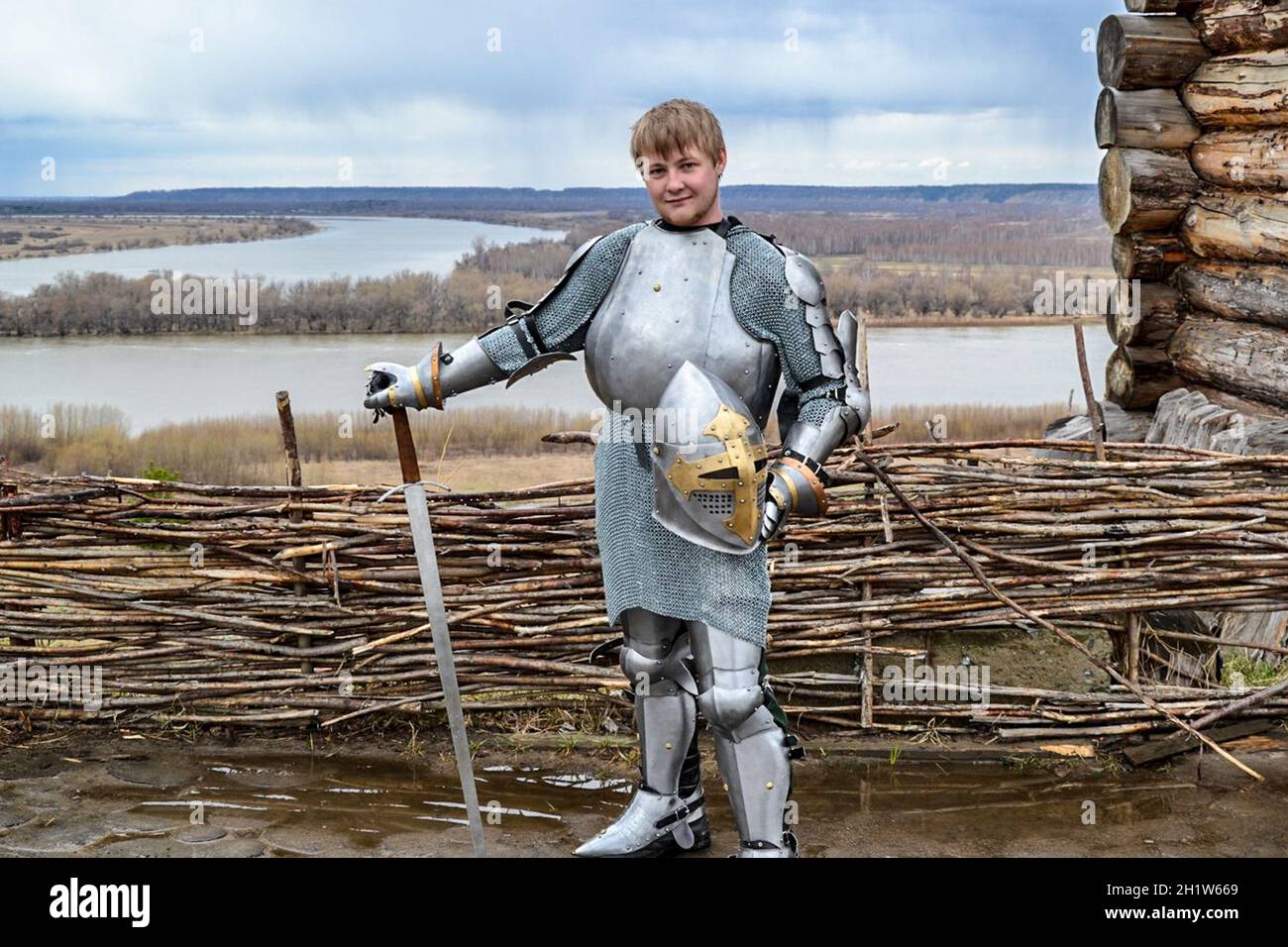 Knight in armor on the background of a wicker fence, a wooden house and ...