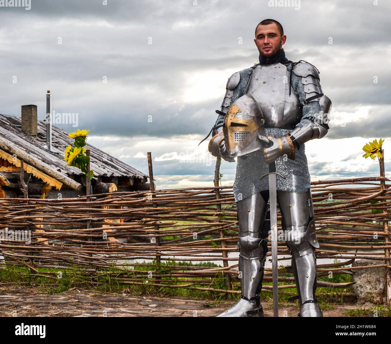 Knight in armor on the background of a wicker fence, a wooden house and ...