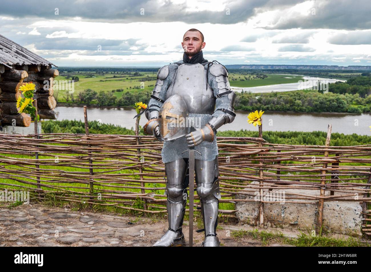 Knight in armor on the background of a wicker fence, a wooden house and ...