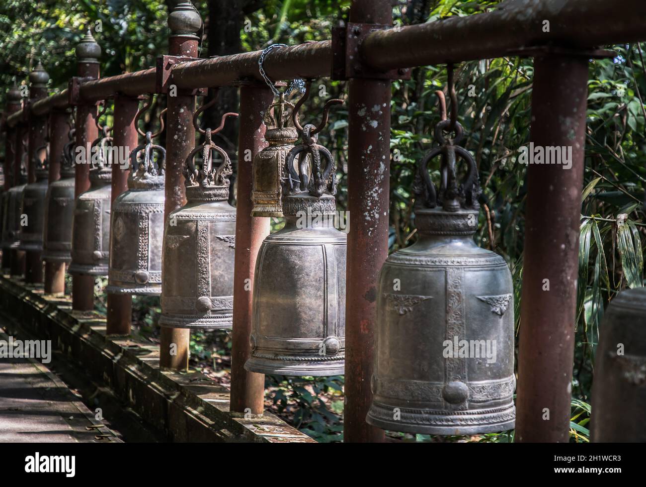 Many metallic bells hanging in a row on wooden pillars outside in thai ...