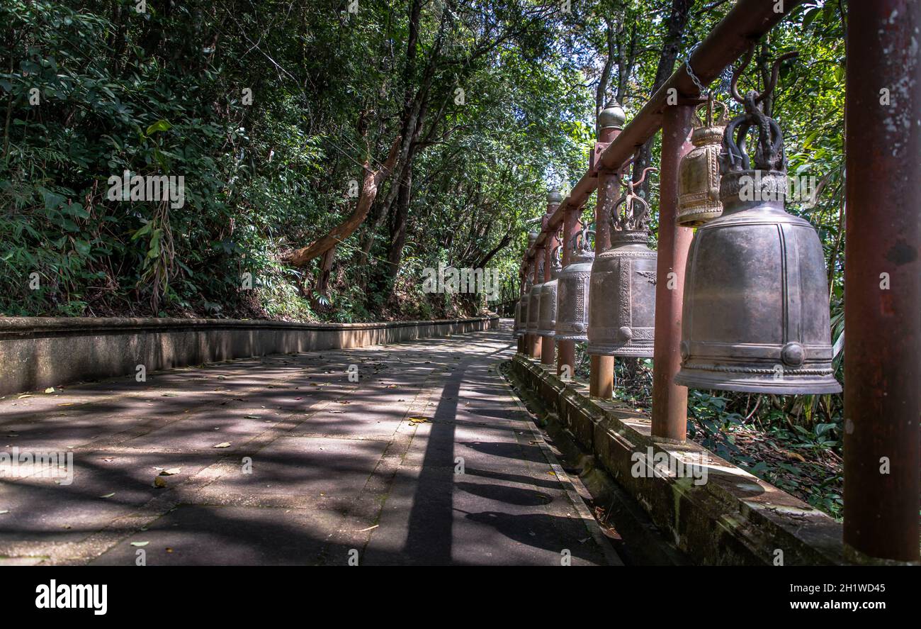 Many metallic bells hanging in a row on wooden pillars outside in thai ...