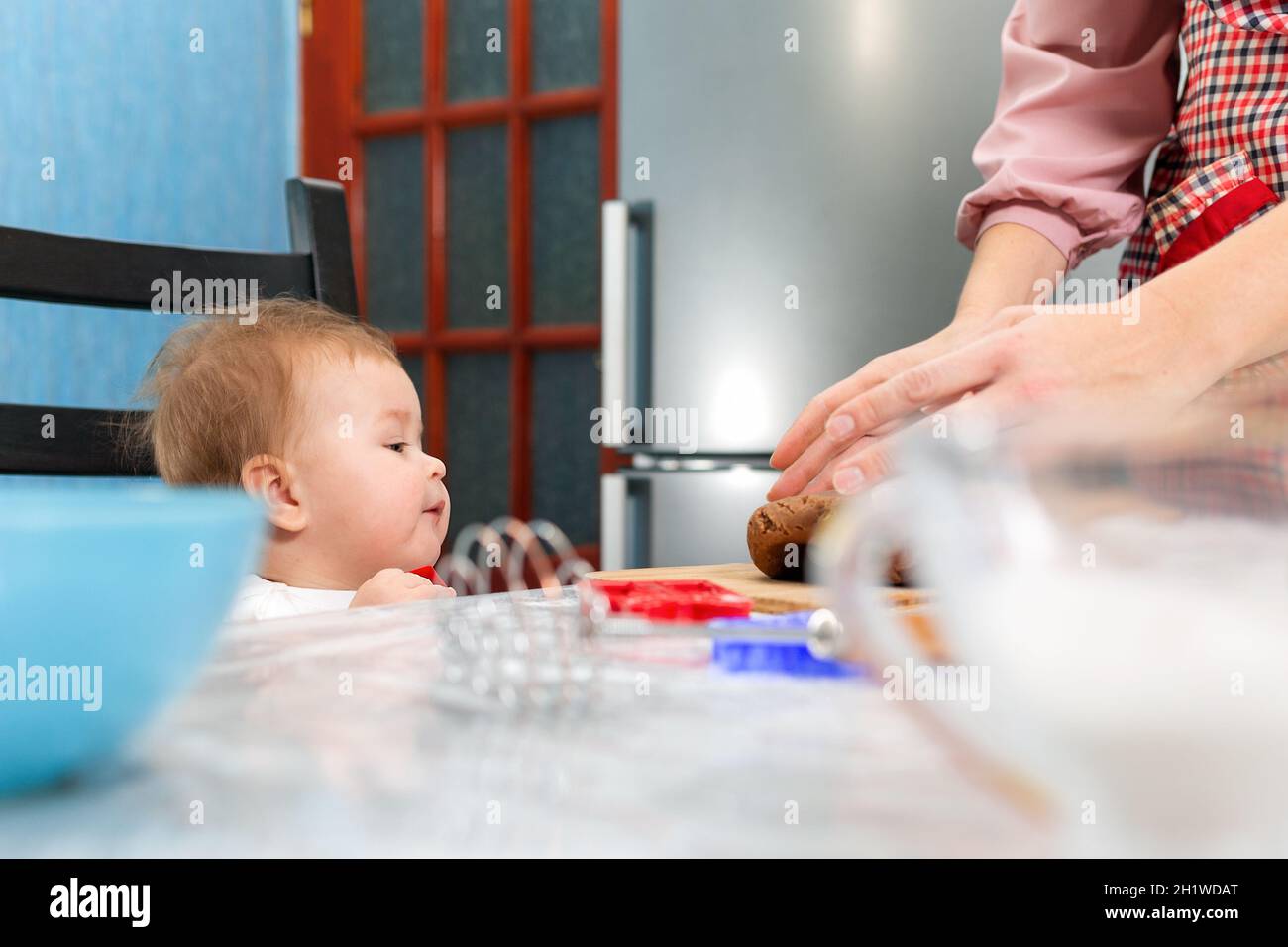 Cute baby is sitting on a chair and watching his mother cook. Side view ...