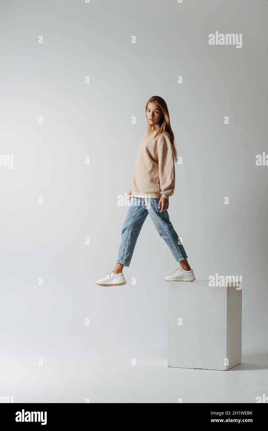 Side image of a teenage girl walking of a white cube, stepping into the air. Giving the ...