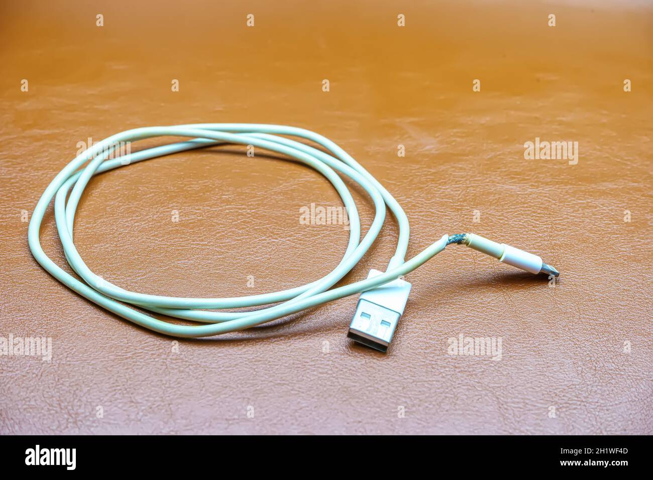 Old smart phone charger cable is damaged on a brown leather background ...