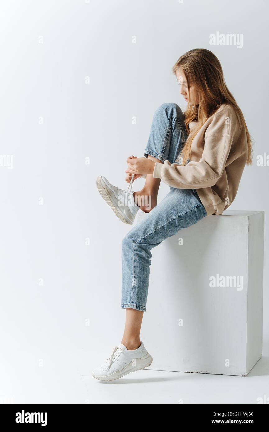 Side view of a teenage girl lacing her sneakers. Sitting on a white ...
