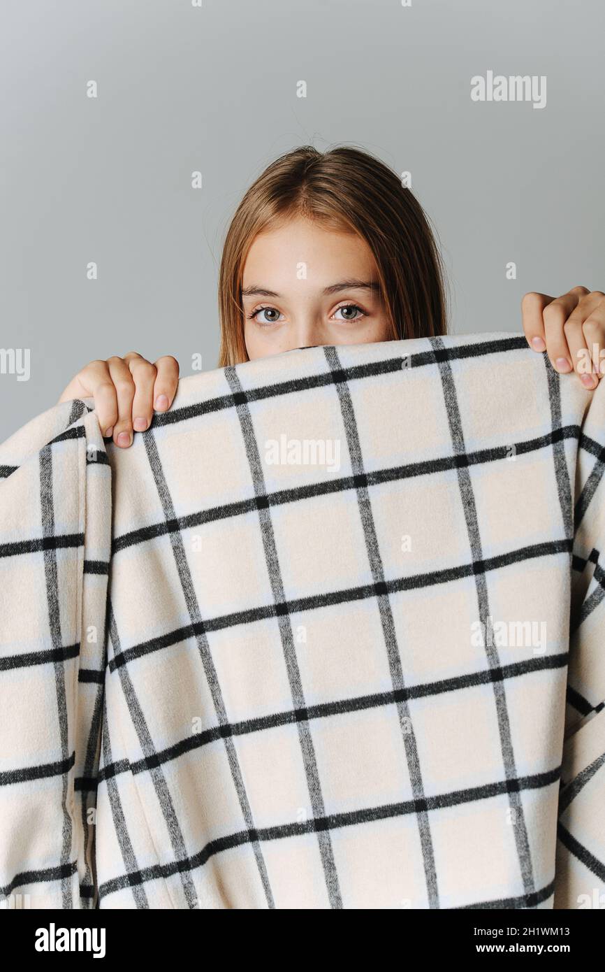Timid teenage girl holding a checkered jacket over her face, peeking ...