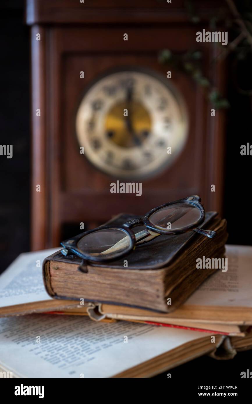 Old holy Bible, books and glasses on wooden table with vintage clock in ...