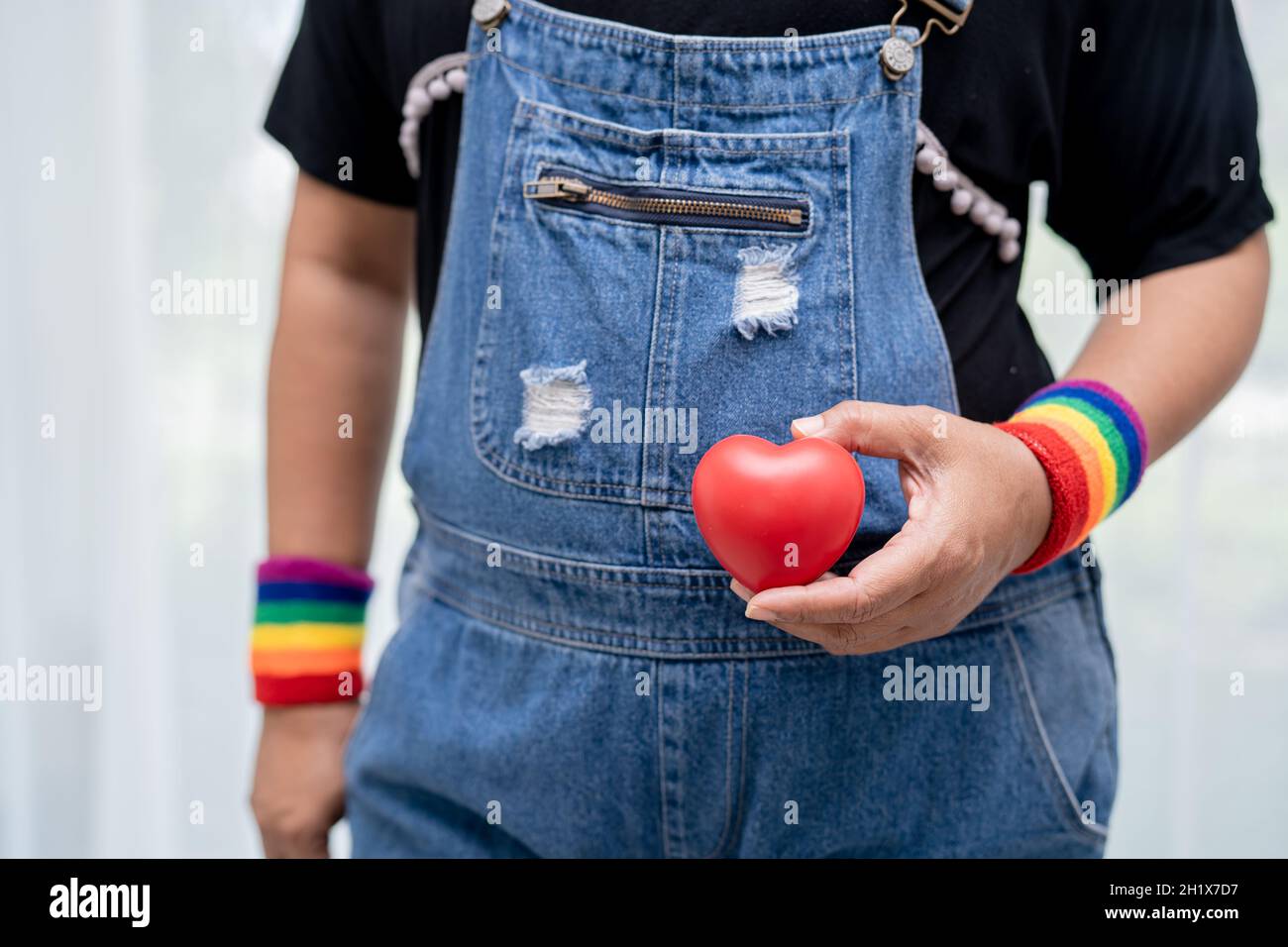 Asian lady wearing rainbow flag wristbands and hold red heart, symbol ...