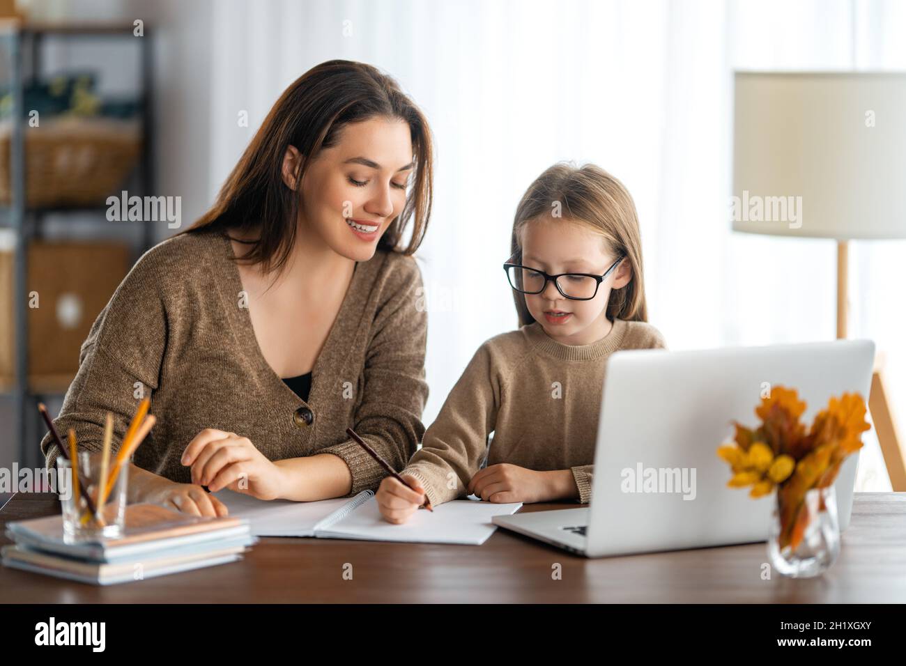 Back to school. Happy child and adult are sitting at desk. Girl doing ...