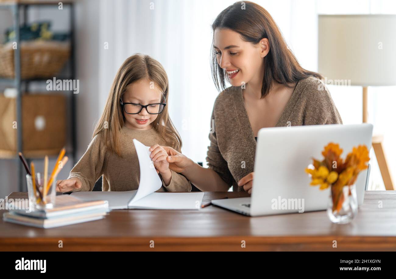 Back to school. Happy child and adult are sitting at desk. Girl doing ...