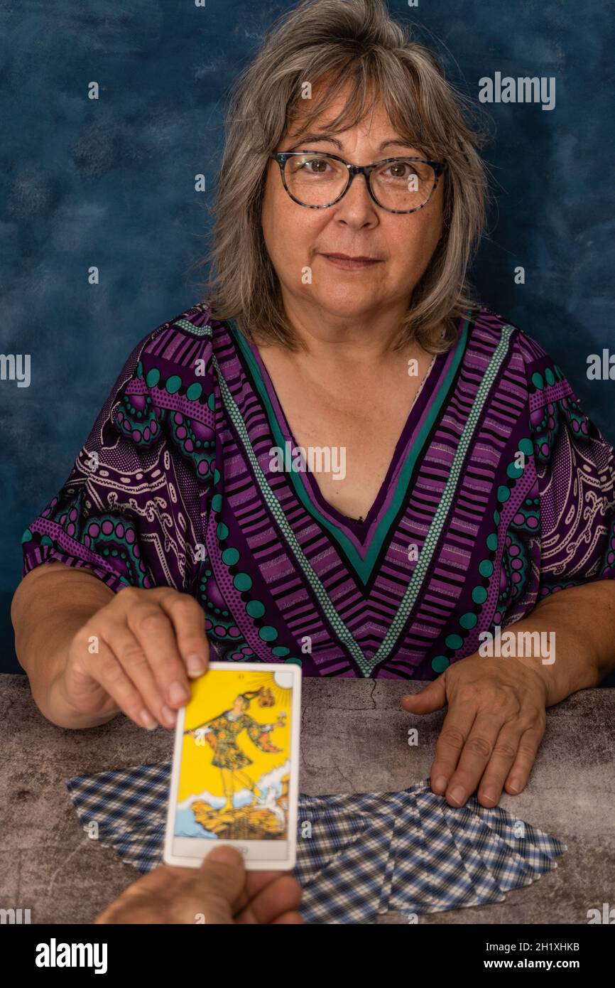older white-haired woman reading tarot cards on a wooden table with ...