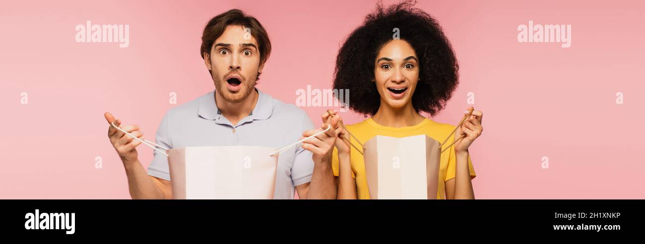 thrilled interracial couple with shopping bags looking at camera ...