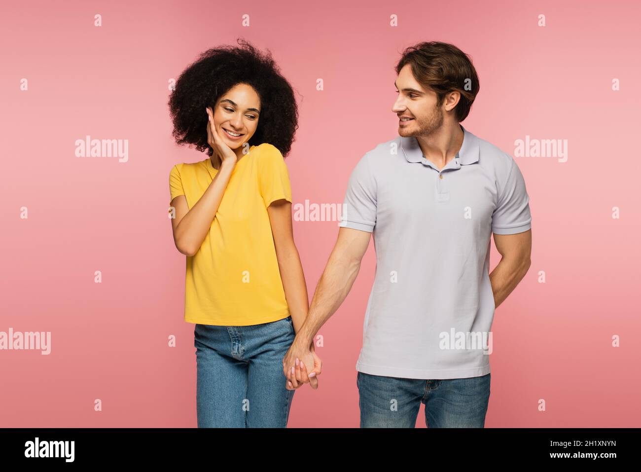 shy hispanic woman holding hands with smiling man hiding something ...