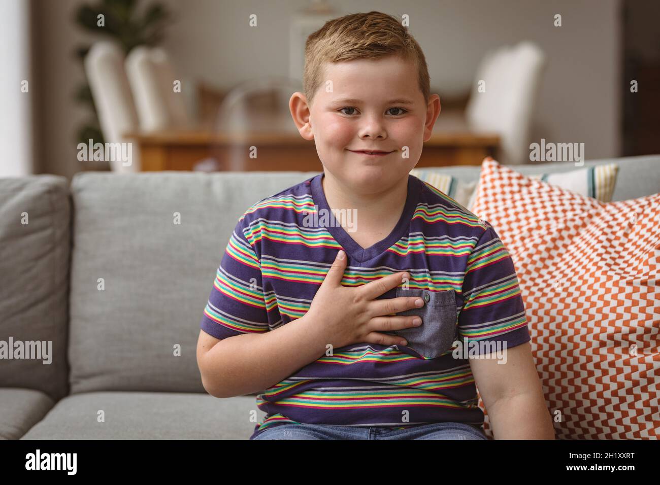 Portrait of caucasian boy making hand gestures sitting on the couch at ...