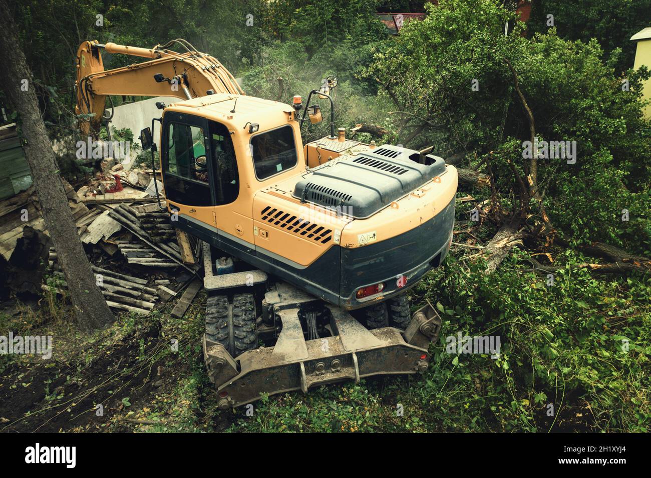 Yellow hydraulic excavator breaks and knocks down green trees on site ...