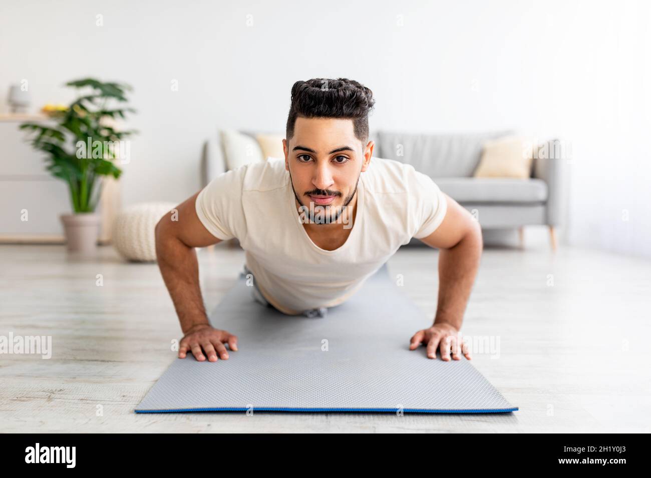 Strong young Arab man making strength workout, standing in plank pose ...