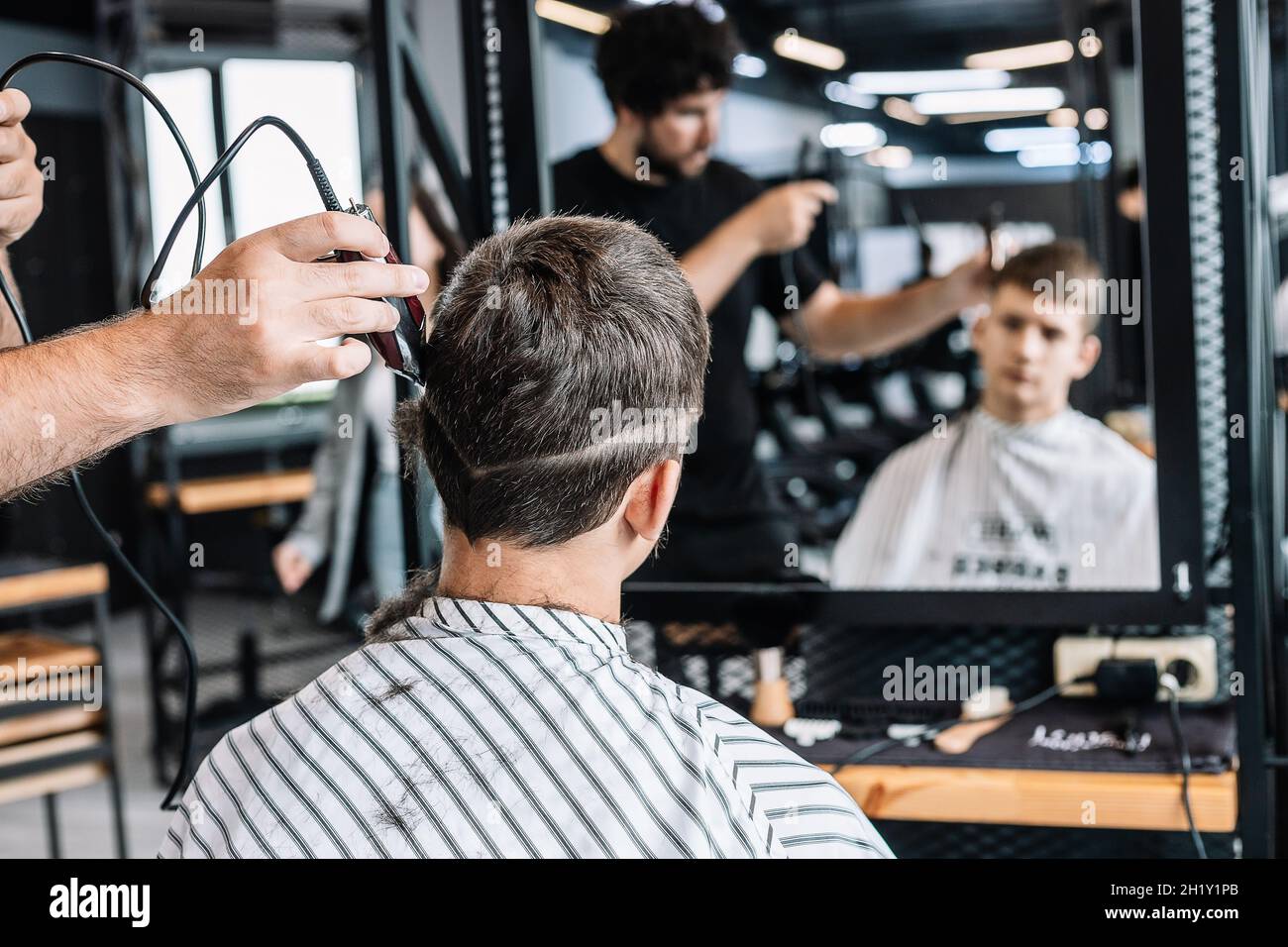 Handsome tall bearded brunette barber gives a trendy haircut to a ...