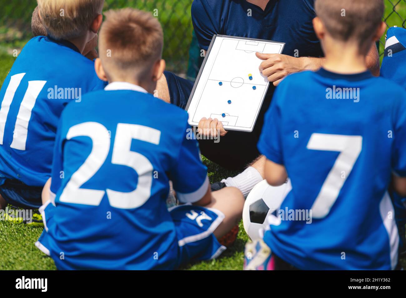 Anonymous football coach teaching kids on grass field. Coach explains a ...