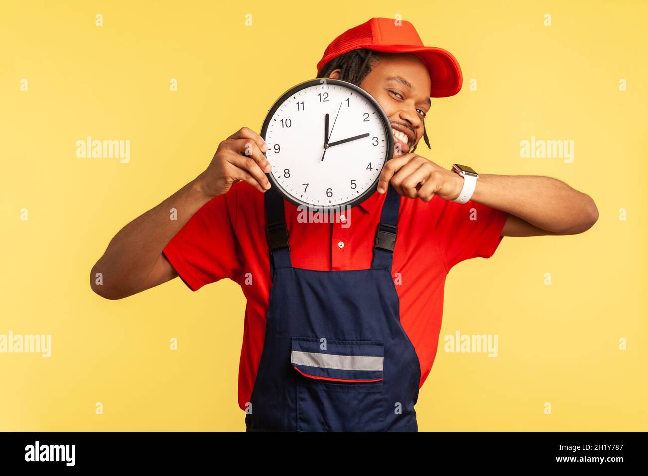 Smiling happy handyman wearing blue uniform holding big wall clock in ...