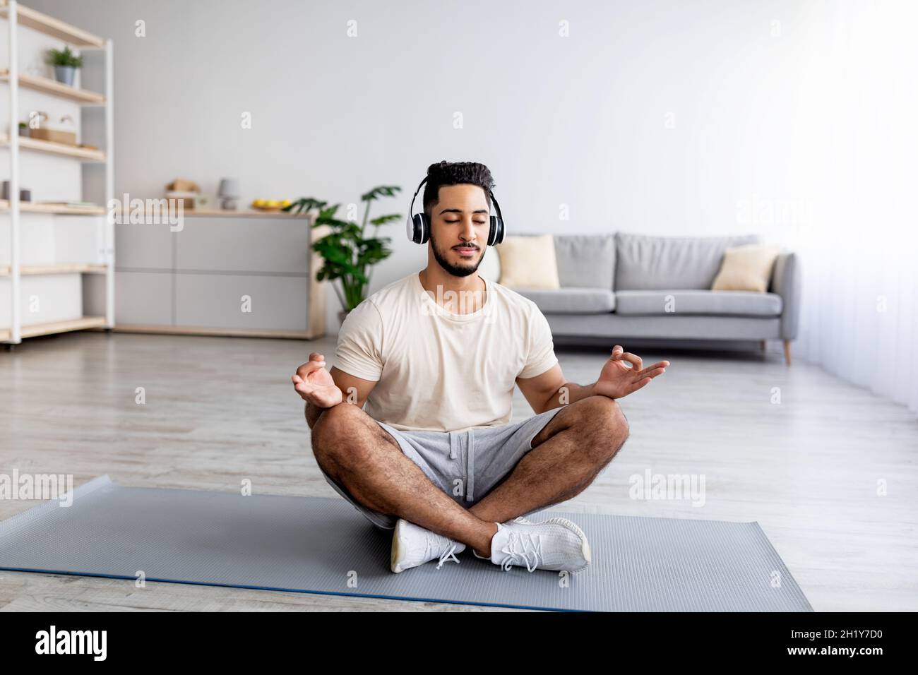 Peaceful young Arab man sitting in lotus pose, wearing headphones ...