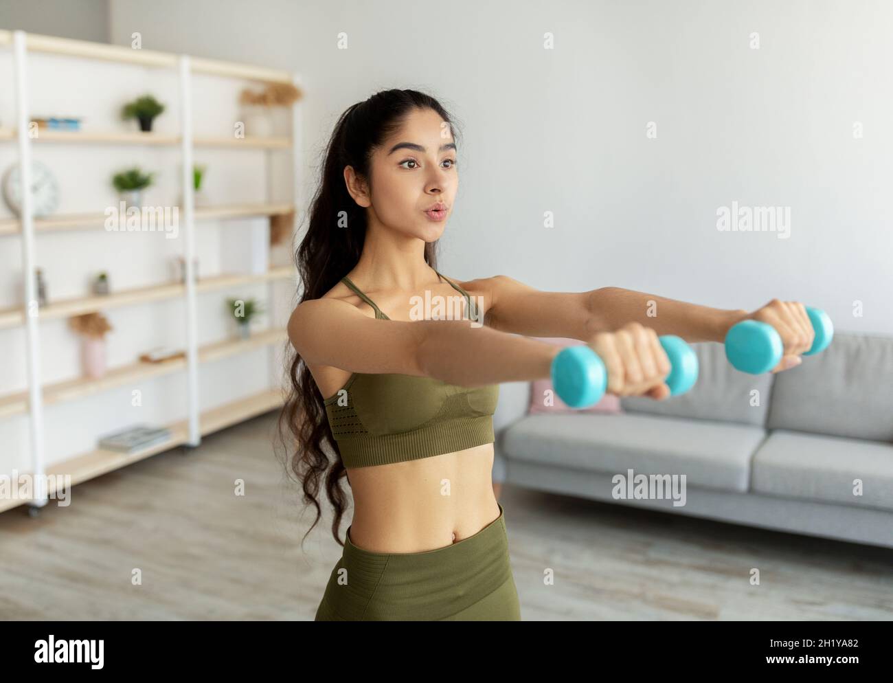 Domestic sports during covid lockdown. Strong Indian woman doing exercises with weights, working ...