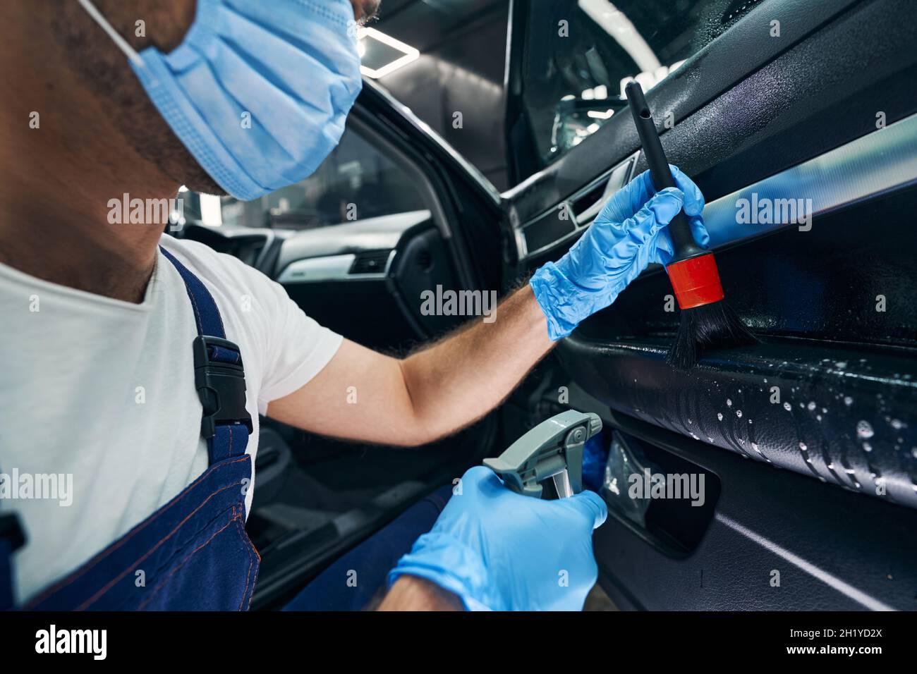 Car mechanic in mask spraying and cleaning auto door Stock Photo - Alamy