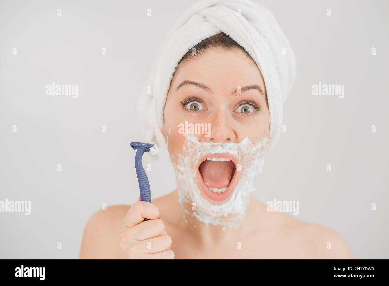 Funny portrait of a woman with shaving foam on her face holding a razor ...