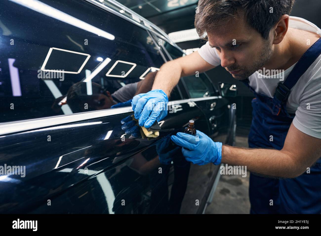 Attentive worker smearing blemishes on auto surface with ceramic ...