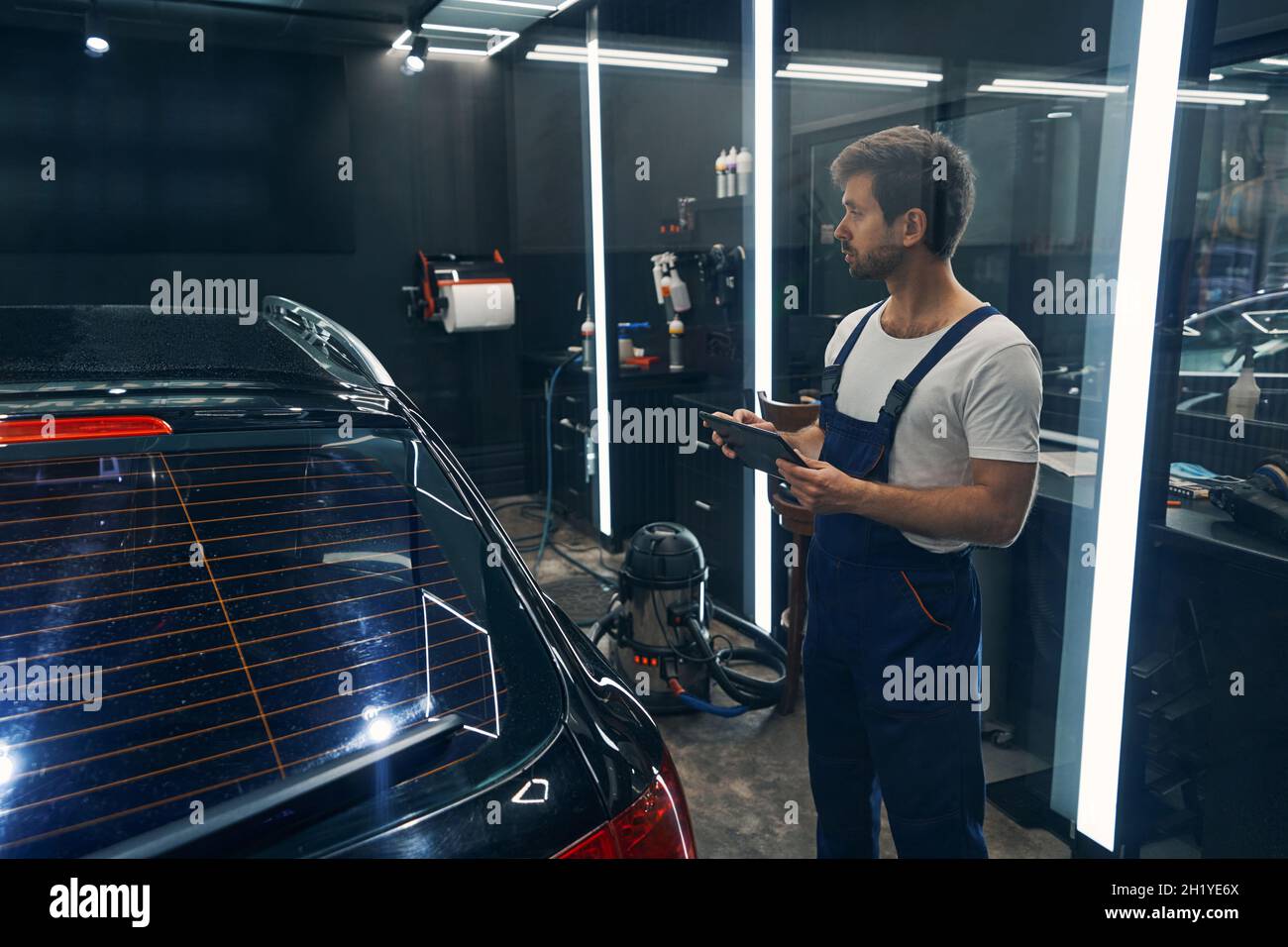 Worker of car service entering information about detailing to tablet ...
