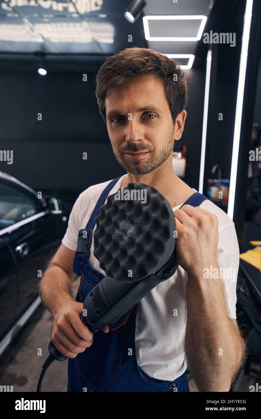 Man car repairman showing sanding machine to camera Stock Photo - Alamy
