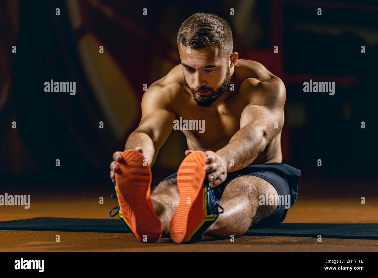 Full-length portrait of young sportive man doing stretching. Gym ...