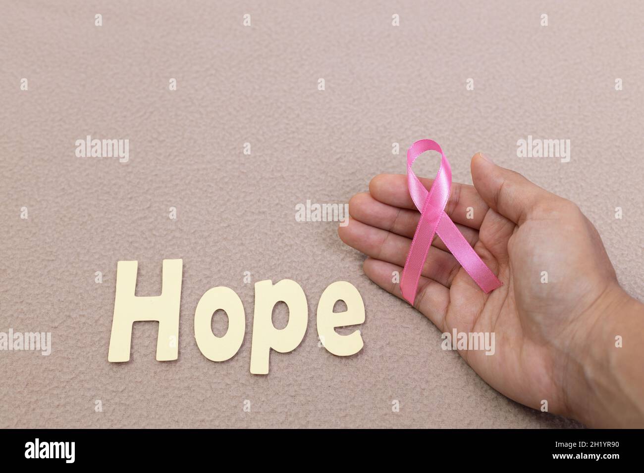 Hand holding a pink awareness ribbon and the word hope on a brown ...