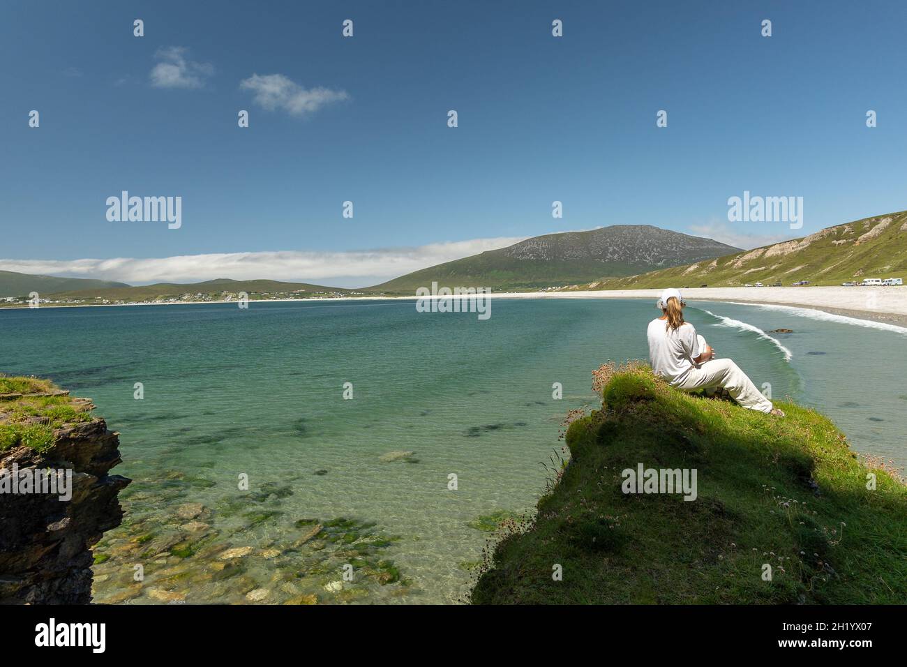 Blonde Caucasian female sitting on a cliff looking at the Irish coast ...