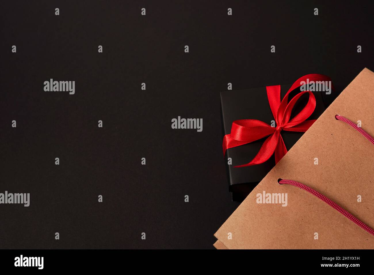 Gift box wrapped in black paper with red ribbon in paper shopping bag ...