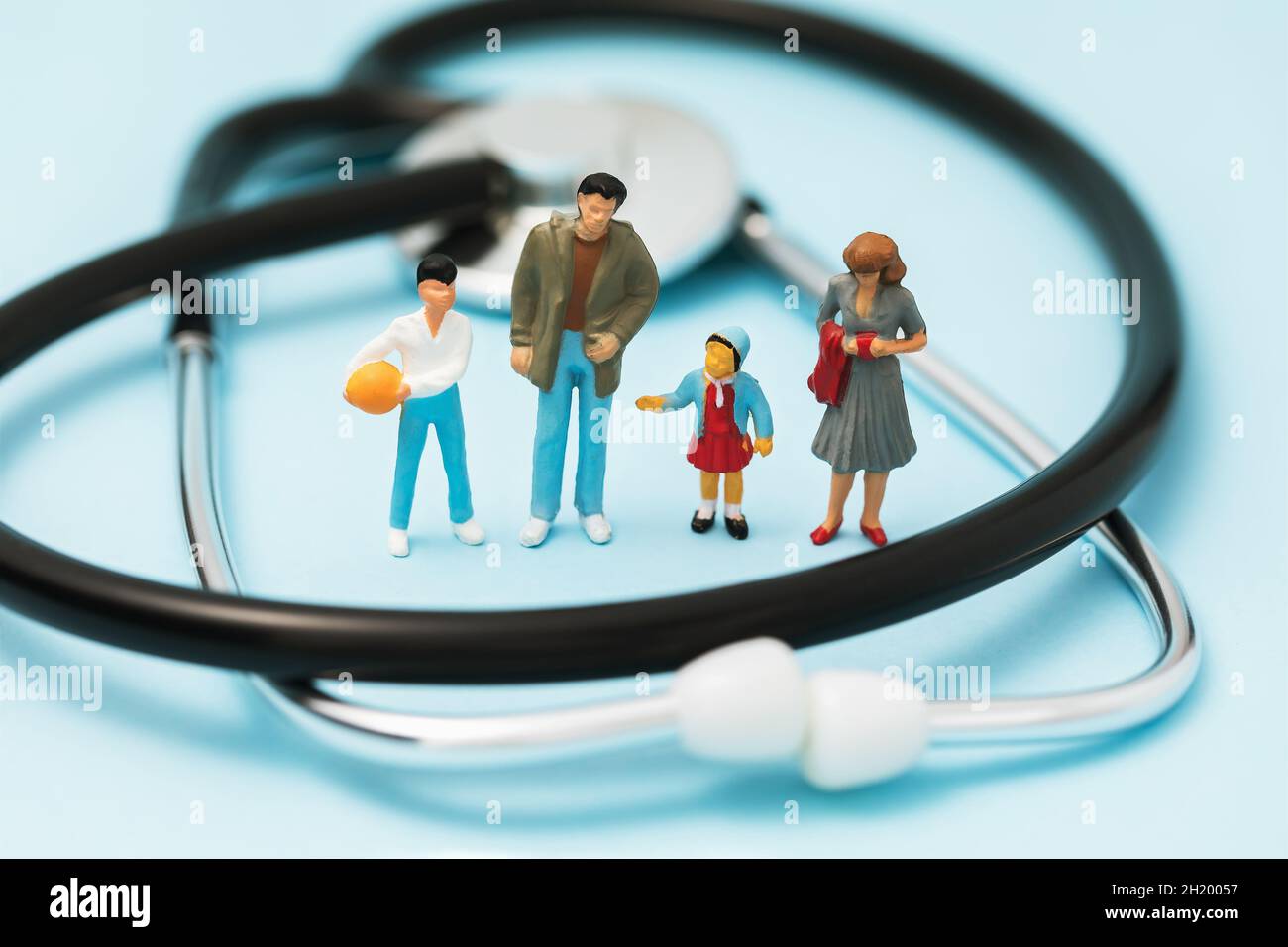 Small plastic toy figures of people and medical statoscope on blue ...