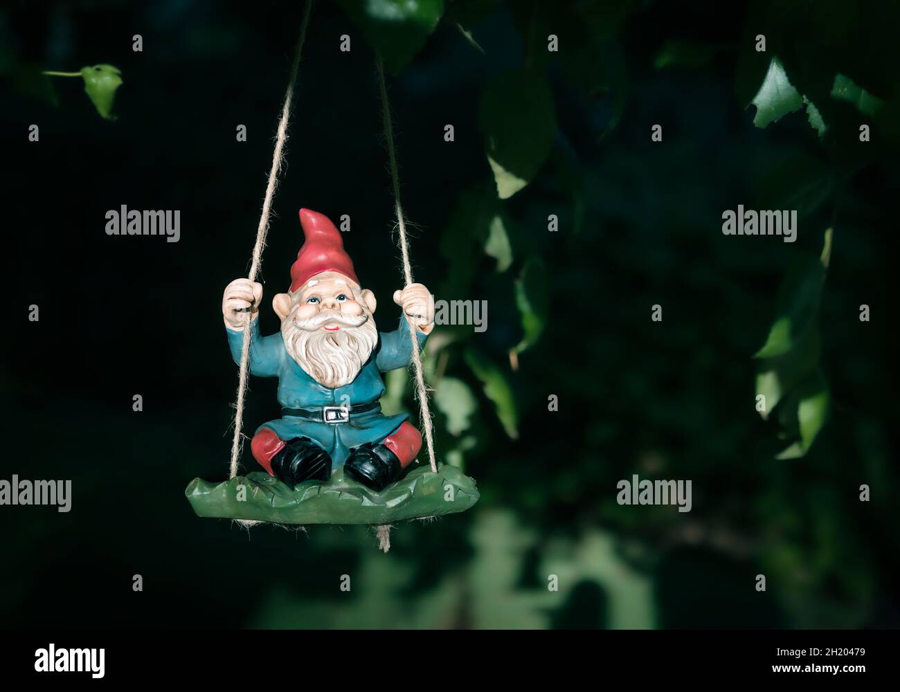Garden dwarf sitting on a swing hanging from a tree , outside in the ...