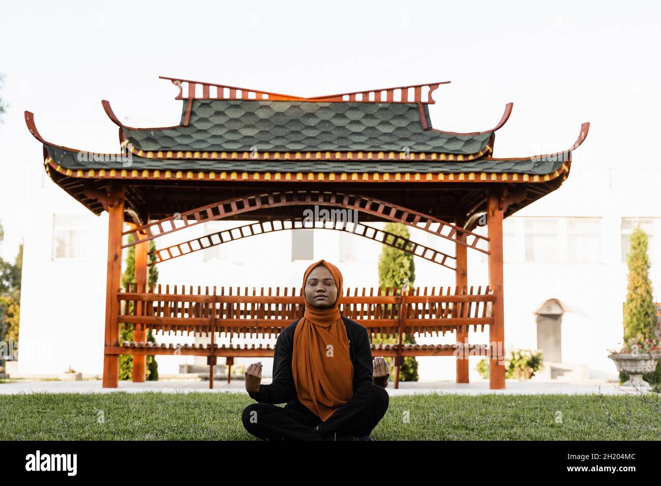 Black muslim woman meditating yoga near chinese arbor. African girl is ...