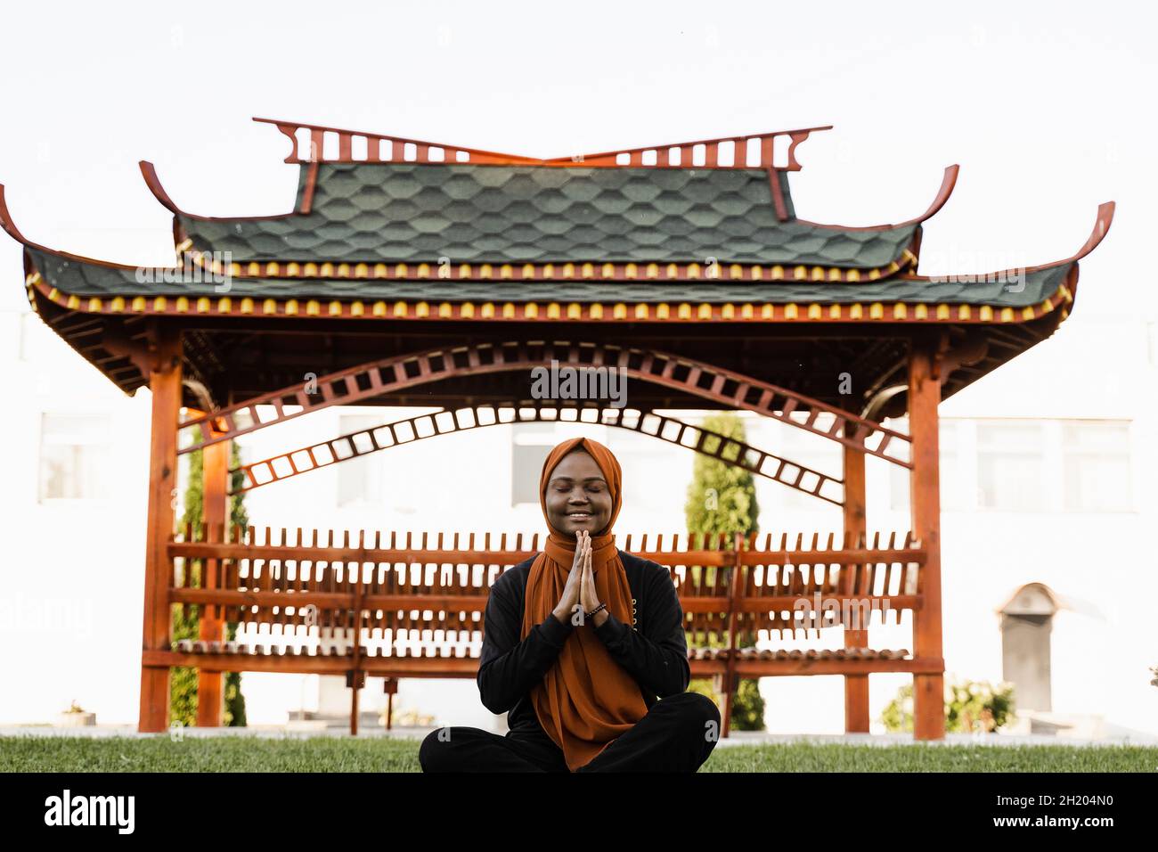 Black muslim woman meditating yoga near chinese arbor. African girl is ...